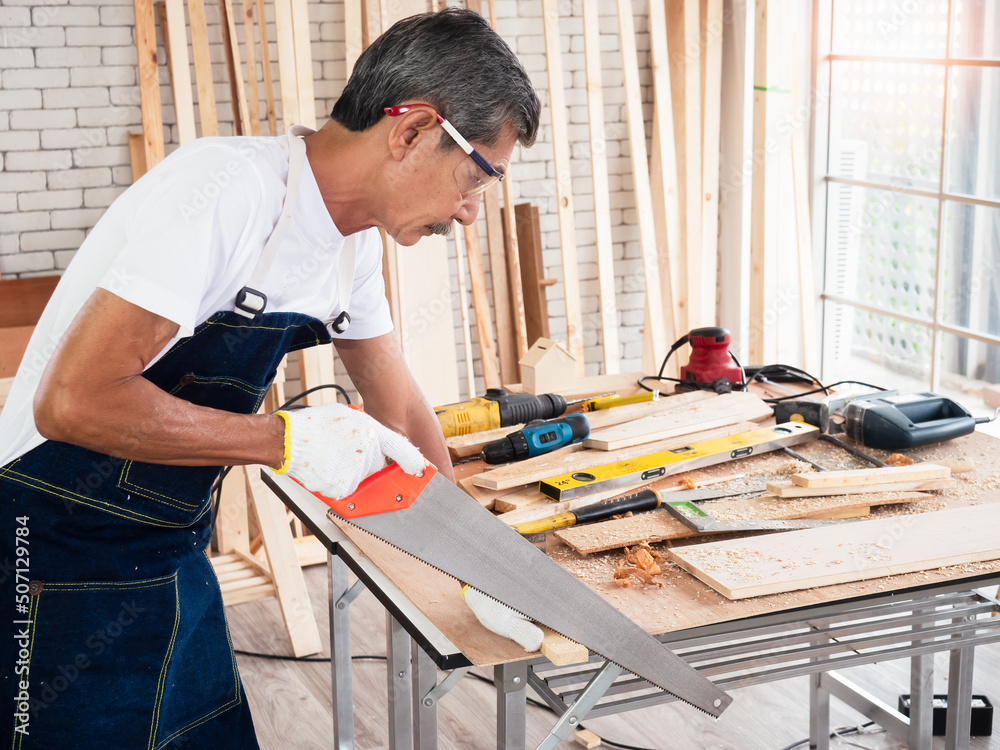 The older carpenter working on woodcraft using a hand saw for ...