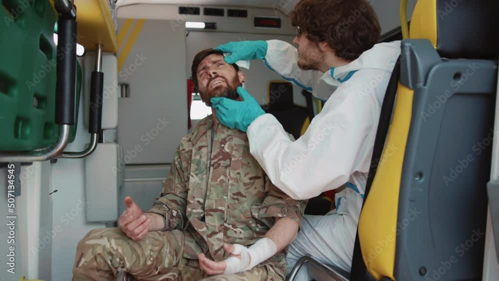 Medic provides medical care to a wounded military man sitting in an ...