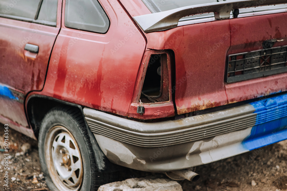 An old, red broken car stands in a landfill after the war in Ukraine in ...