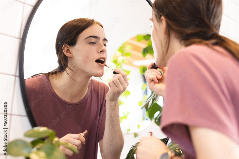 Non-binary trans woman putting lipstick looking in the mirror in ...