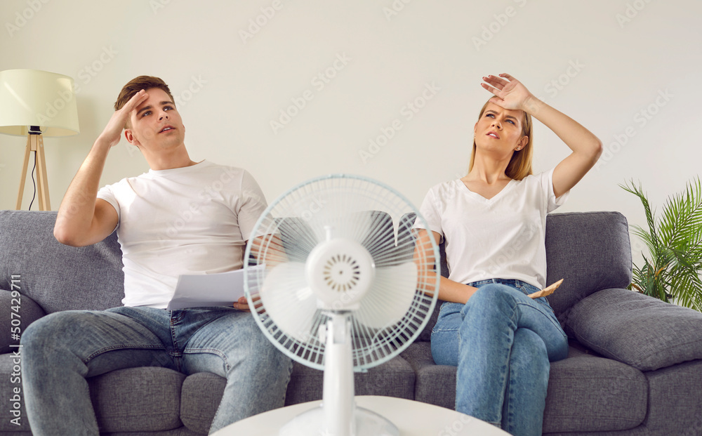 Exhausted woman and man sitting in front of electric fan sweating ...