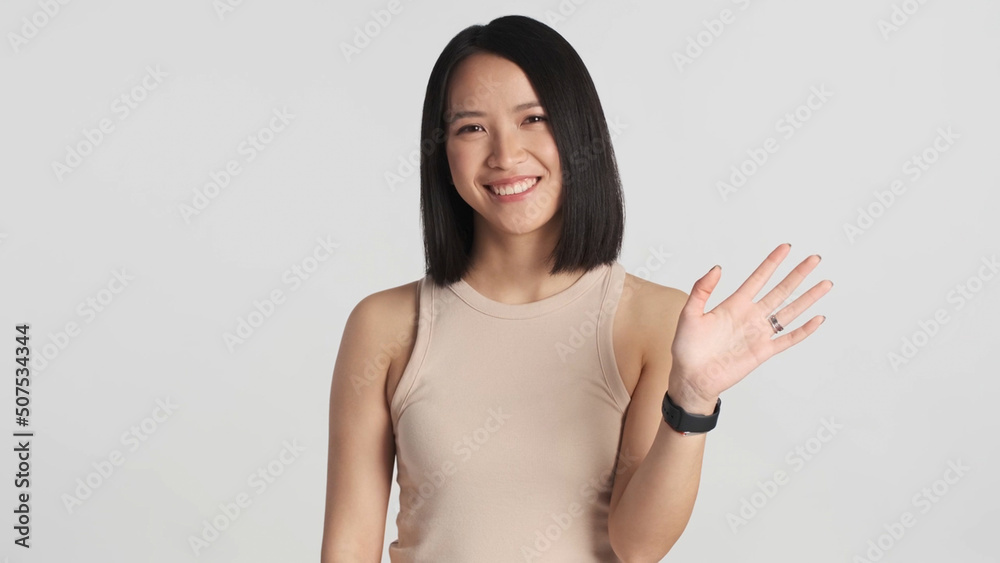 Beautiful Asian woman looking happy waving hello to friend isolated on ...