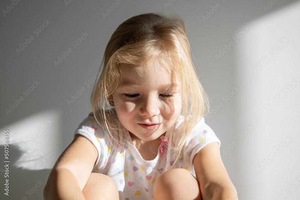 Sad child girl blonde with disheveled hair on the background of a white ...