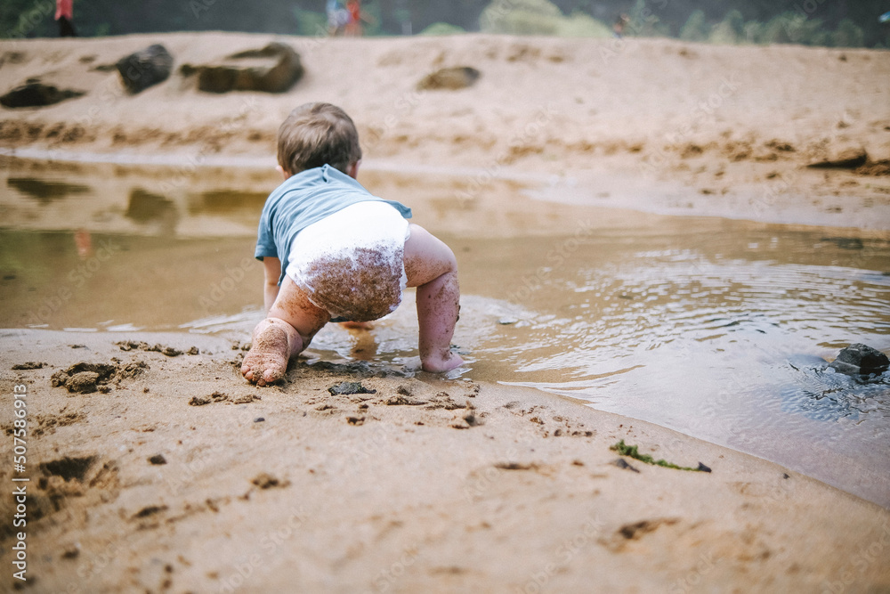 Bebé gateando hacia el agua en la playa, con las piernas y el pañal ...