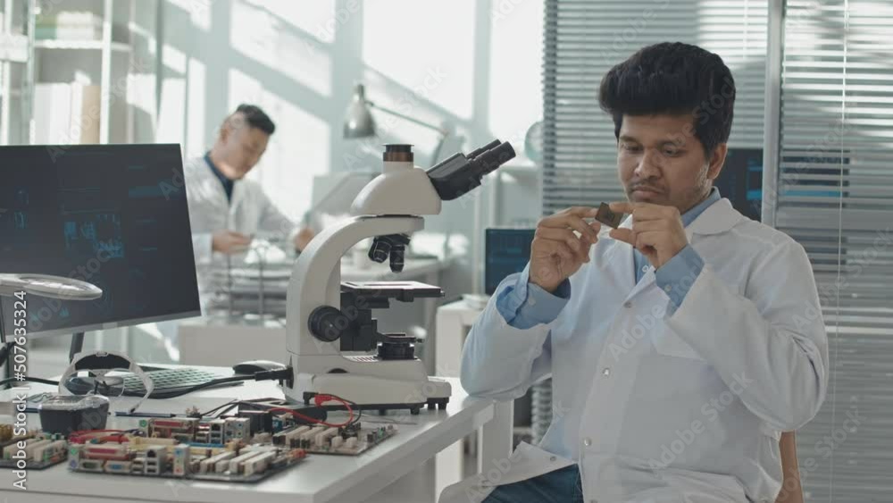 Medium slowmo of serious male Biracial engineer in white lab coat using ...