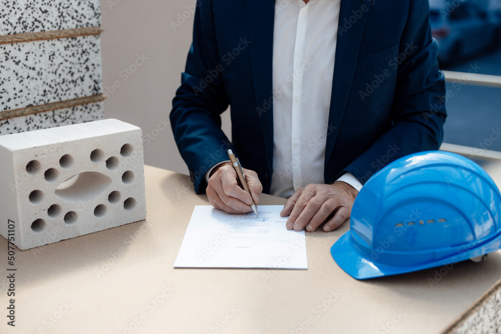 Senior businessman signing document amidst concrete brick and hardhat ...