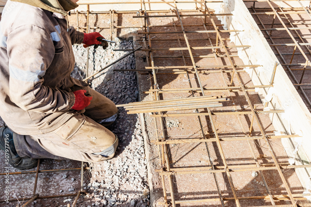 A worker uses steel tying wire to fasten steel rods to reinforcement ...