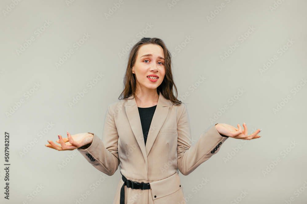 Puzzled woman in smart casual clothes stands on a beige background and ...