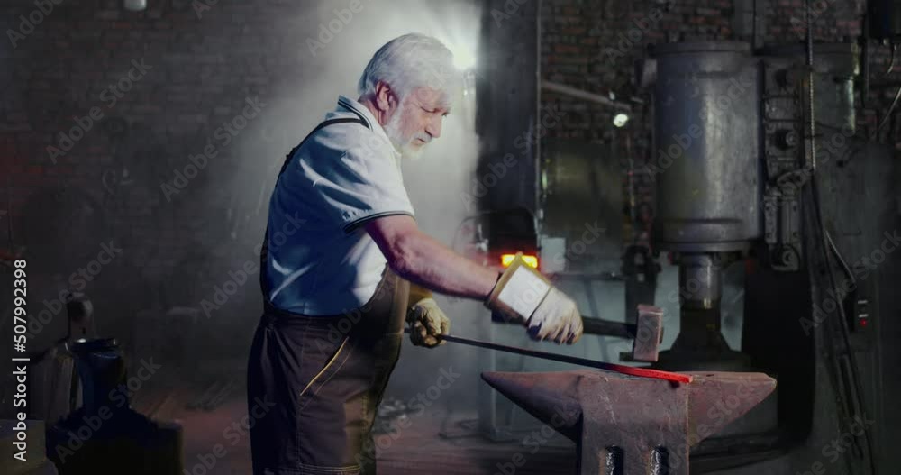Side view of skillful blacksmith working in mastershop. Old strong male ...