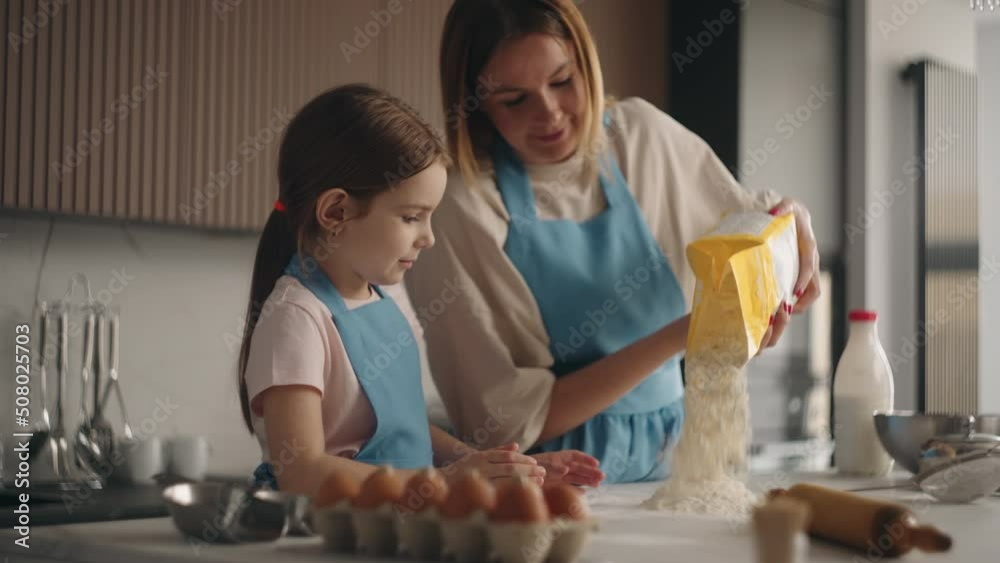 mother and child are cooking in home, woman is pouring flour on table ...