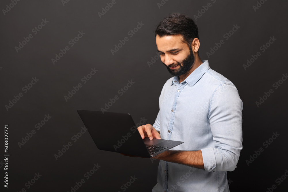 Indian bearded freelancer guy using laptop computer isolated on black ...