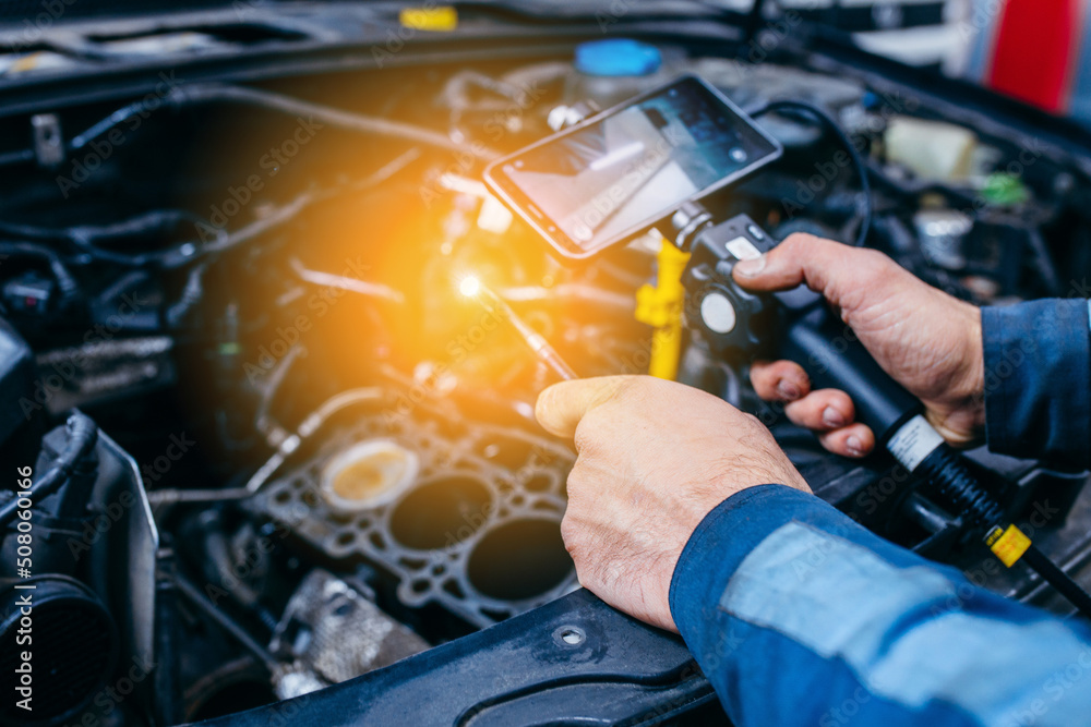 Hands of car mechanic check the vehicle engine with technical endoscope ...
