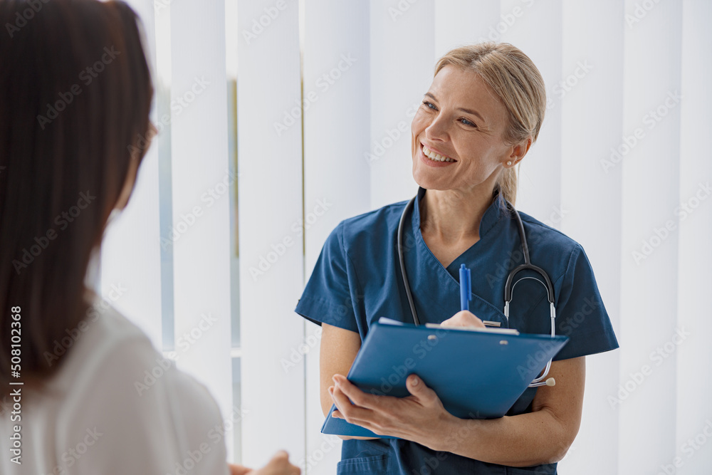 Smiling woman doctor taking notes on clipboard and looking on patient ...