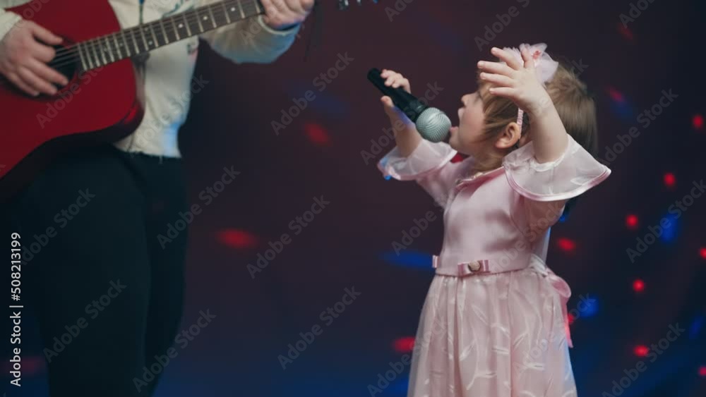 Little girl on stage in vintage dress, she sings into microphone and ...