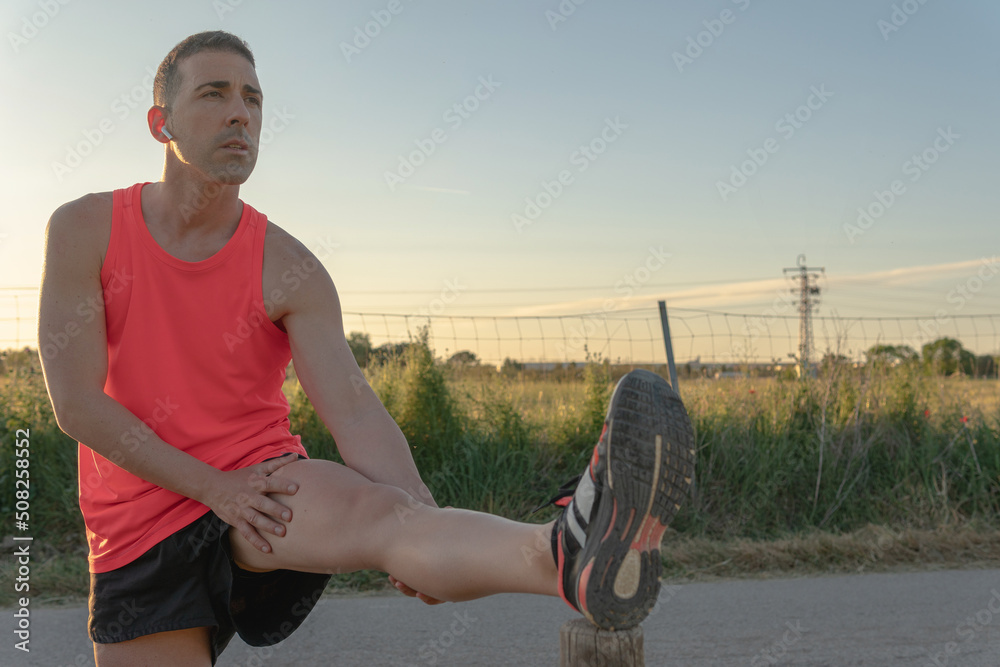 Young runner man relaxing one leg on a wooden post. Side view of a ...