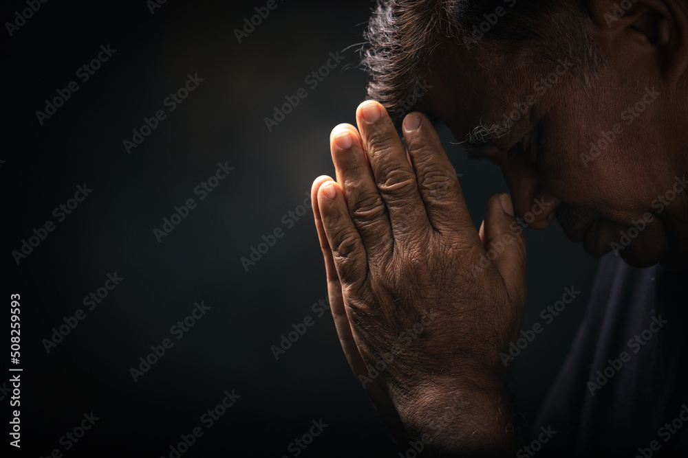 Elderly Asian man bowed his head praying to God on a black background ...