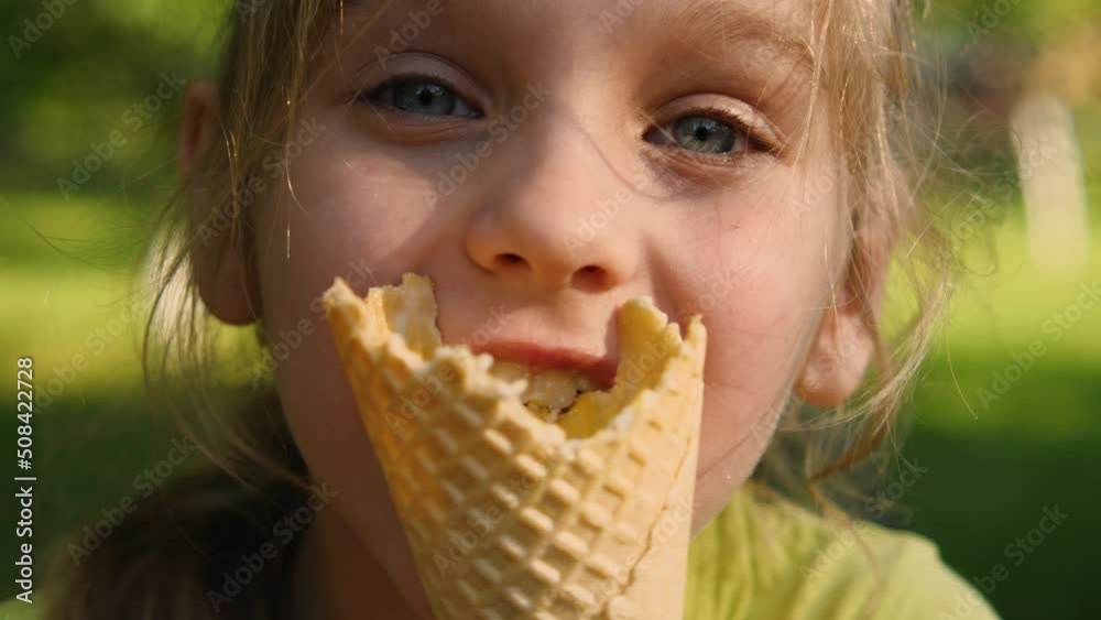 Close-up of a beautiful girl with big blue eyes chewing on an ice cream ...