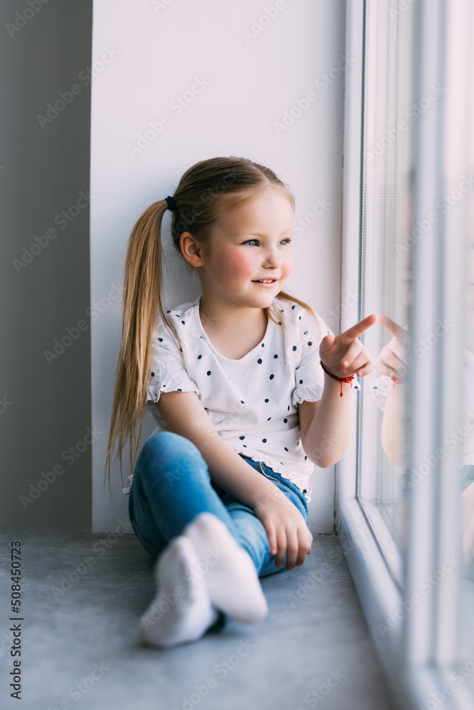 Beautiful little girl smiling and watching out the window. A child ...