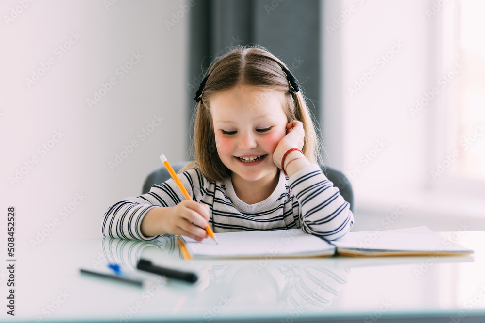 Cute little girl doing homework, reading a book, coloring pages ...
