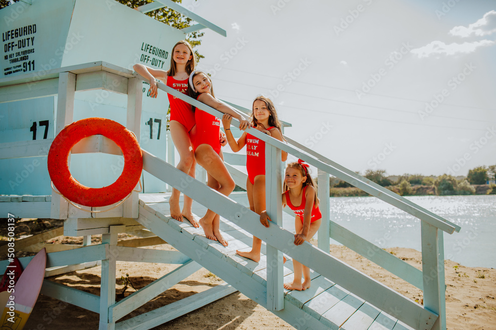 Four pretty young girls in red summer bikini posing on blue lifeguard ...