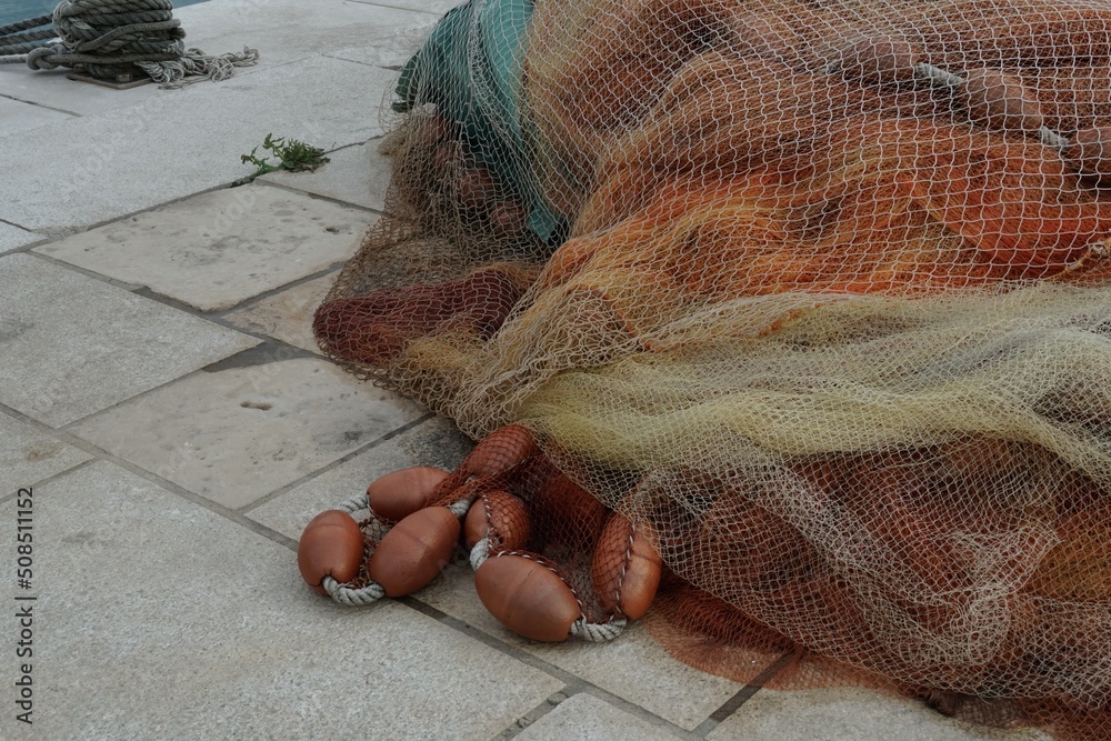 Red fishing net with red-brown floats piled on the pavement in port ...