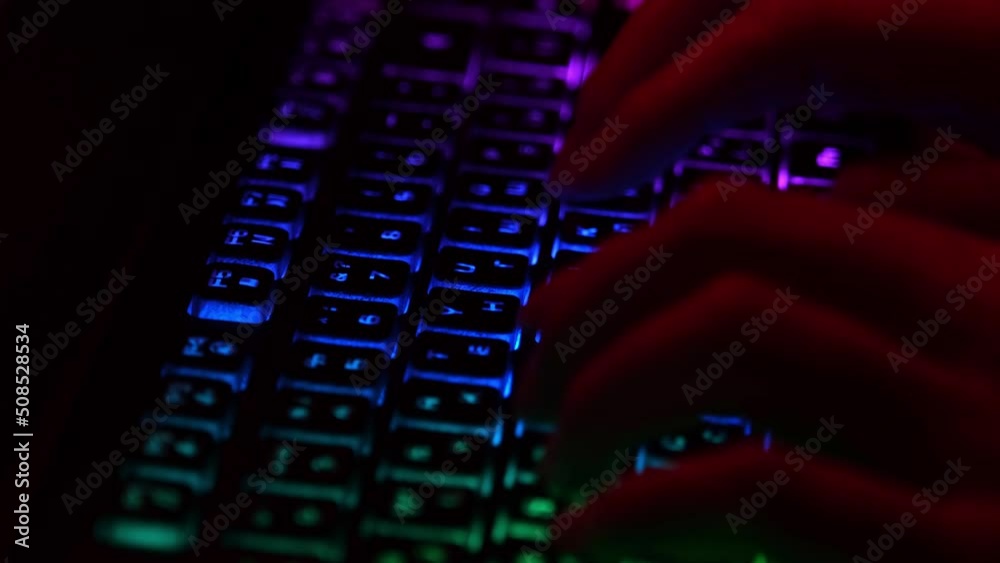 Fingers illuminated by red light type on the keyboard. Multicolored ...