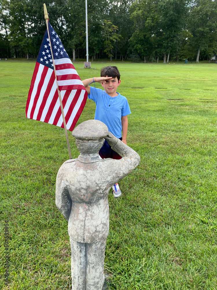 Young child saluting the American flag in front of a saluting statue ...