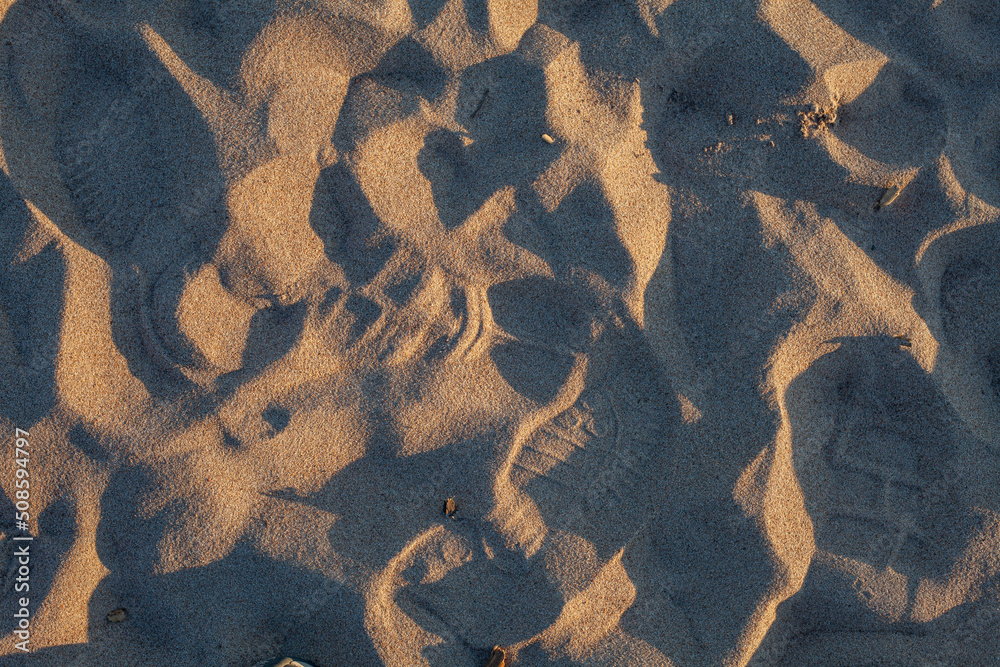 Sand texture with shades in golden hour. Waves and foot prints on beach ...