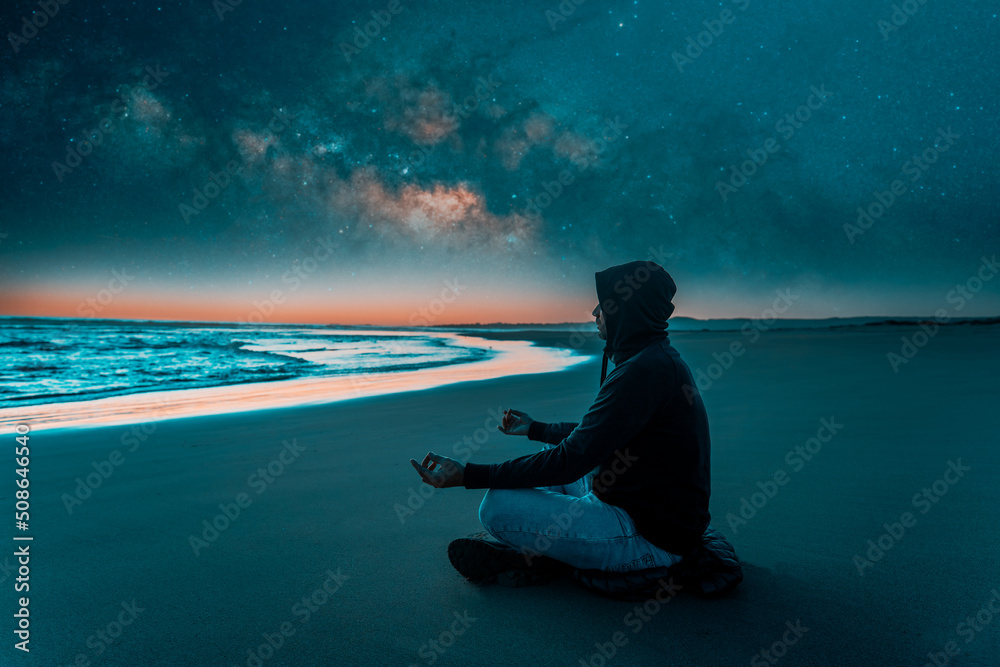 silhouette of a person meditating alone on the beach at night with the ...