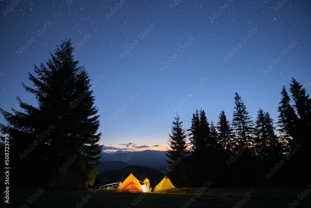 Bright illuminated tourist tents glowing on camping site in dark ...