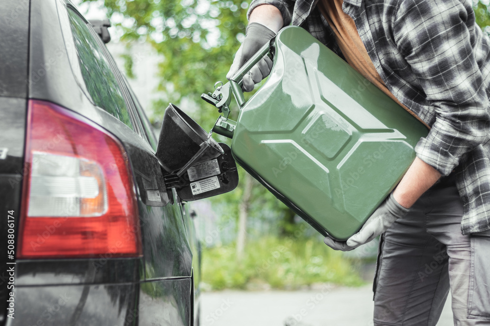 a man pours gasoline from a canister directly into the tank of a car ...