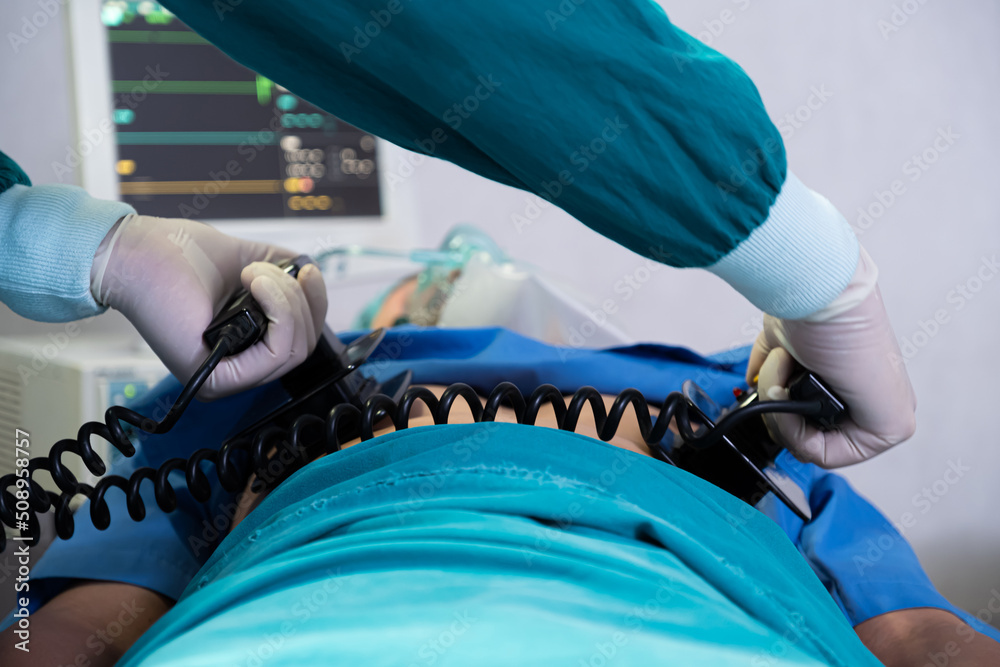 Doctor and nurse using defibrillator to pump at chest of unconscious ...
