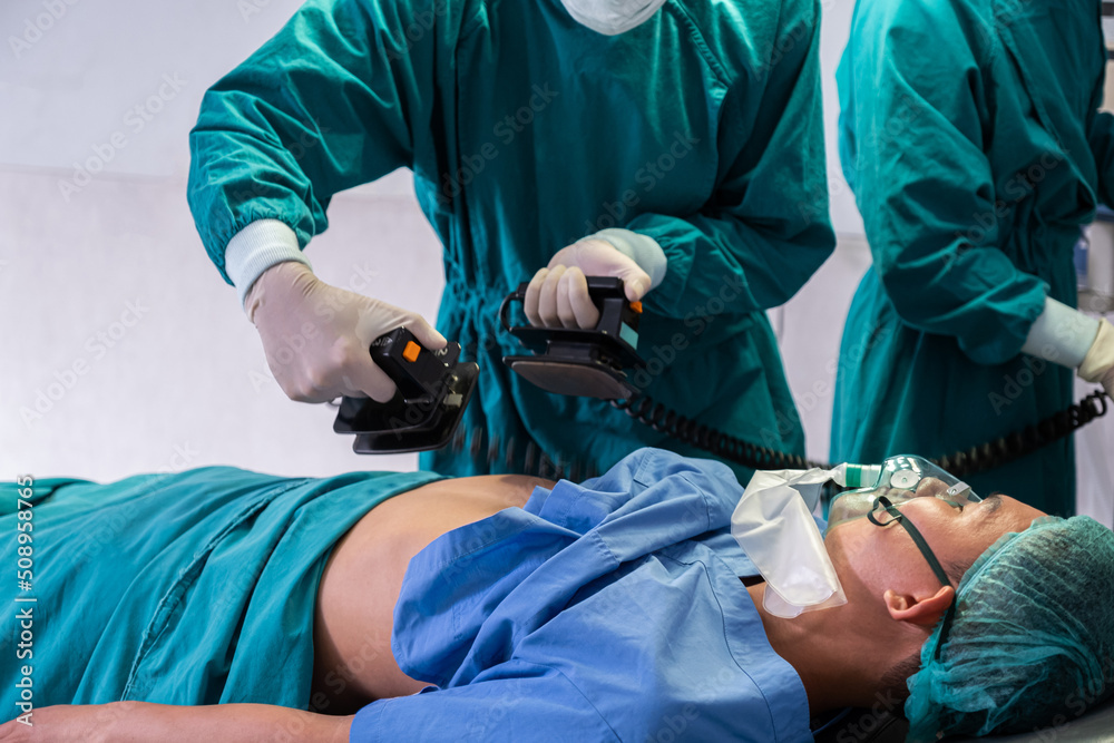 Doctor and nurse using defibrillator to pump at chest of unconscious with low heart rate patient ...