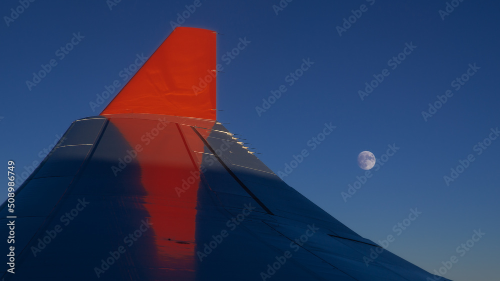 Full moon on a dark sky under the wing of an airplane with a red ...