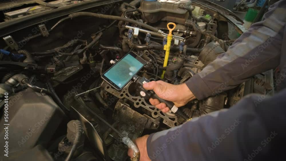 Hands of car mechanic check the vehicle engine with technical endoscope ...