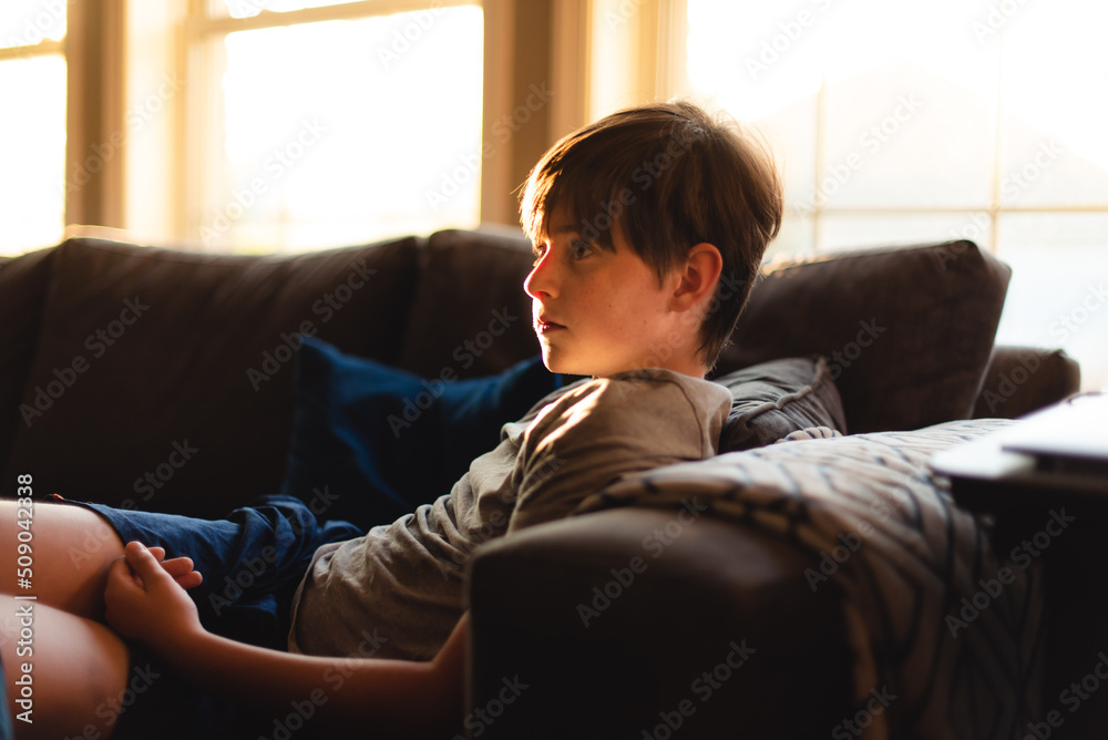 Boy sitting and relaxing on couch in warm window light at home. Stock ...