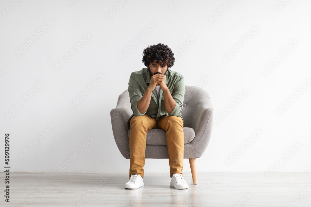 Depressed indian guy sitting in armchair over white Stock Photo | Adobe ...