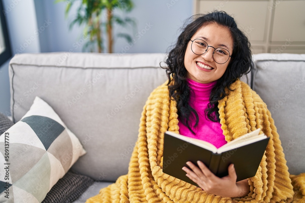 Young chinese woman reading book sitting on sofa at home Stock Photo ...