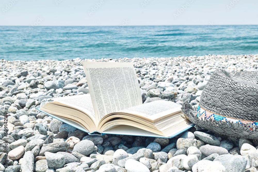 Open book and male straw hat on the pebble beach. Concept of reading ...