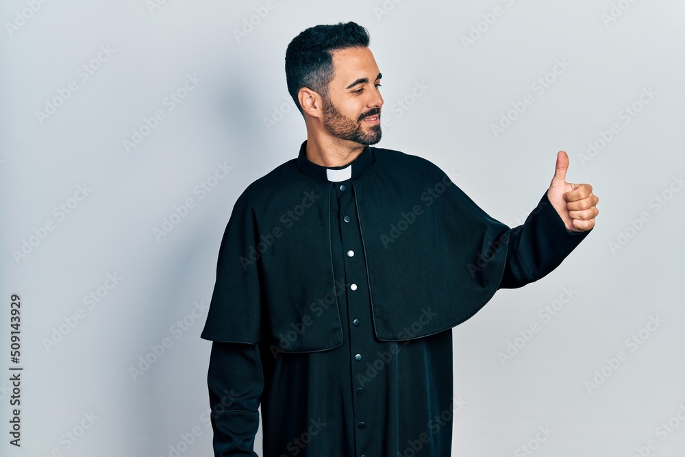 Handsome hispanic man with beard wearing catholic priest robe looking ...