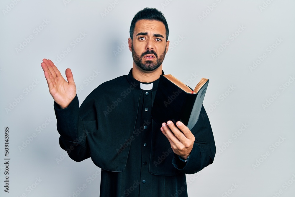 Handsome hispanic priest man with beard holding bible and christian ...