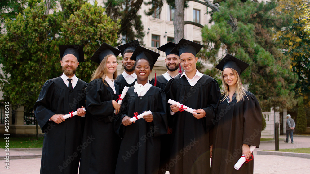 In front of the camera posing group of multiracial students graduates ...