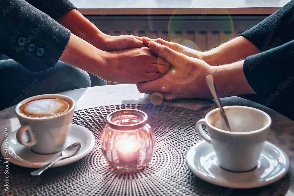 clasped hands of a loving couple over a table in a cafe with two ...