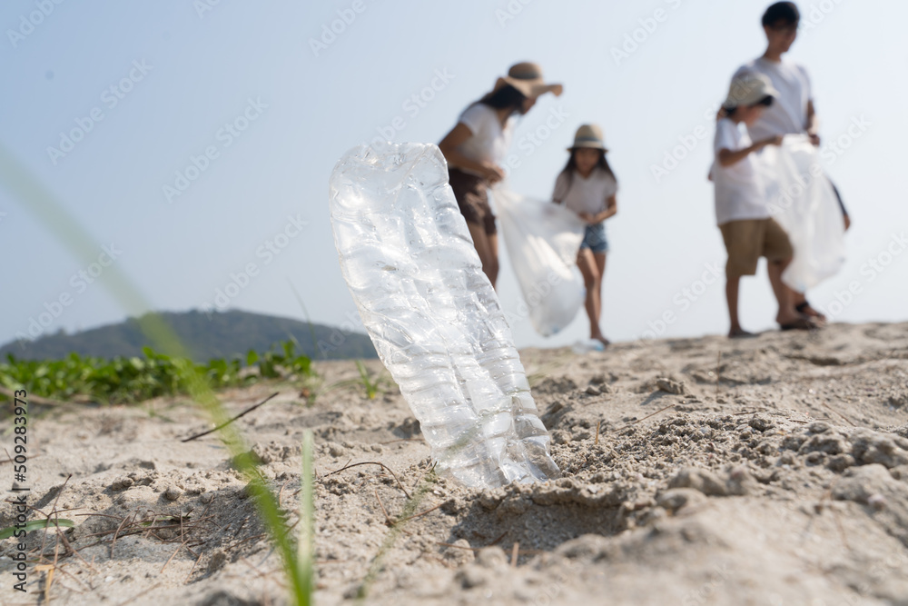 Asian Family volunteer picking up a plastic bottle on a beach with a ...