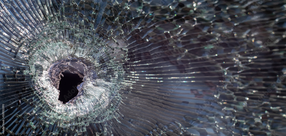 Bullet hole in glass with cracks, real bullet hole close-up. The bullet made a cracked hole in ...