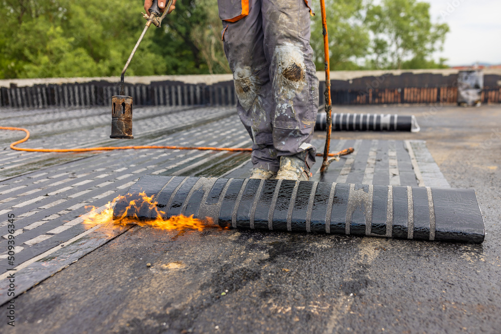 Workers placing a vapor barrier on the roof using a propane gas torch ...