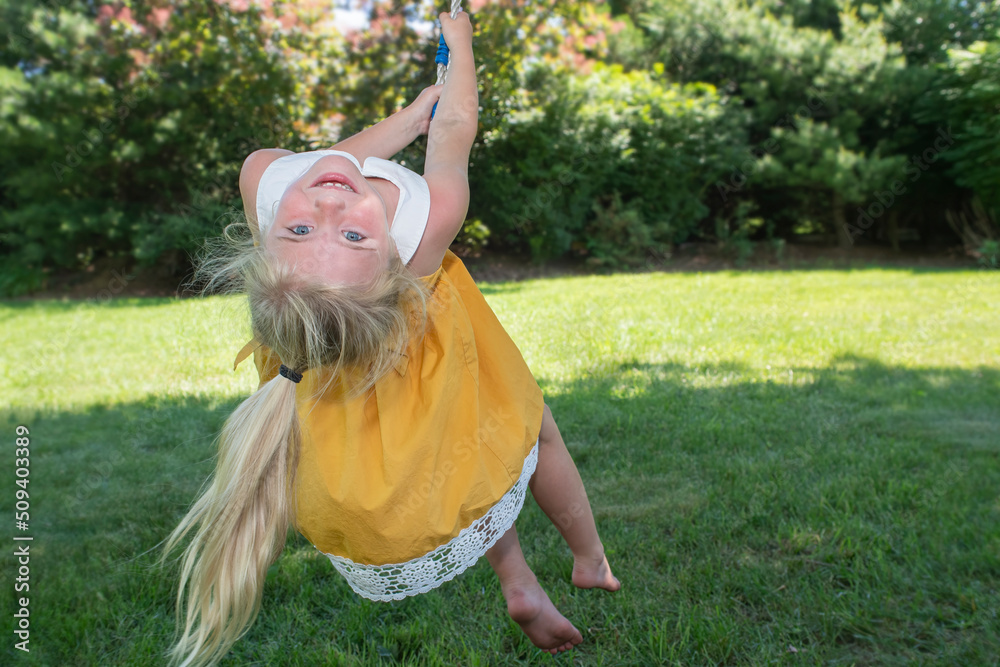 Little girl hanging upside down on a rope swing Stock Photo | Adobe Stock