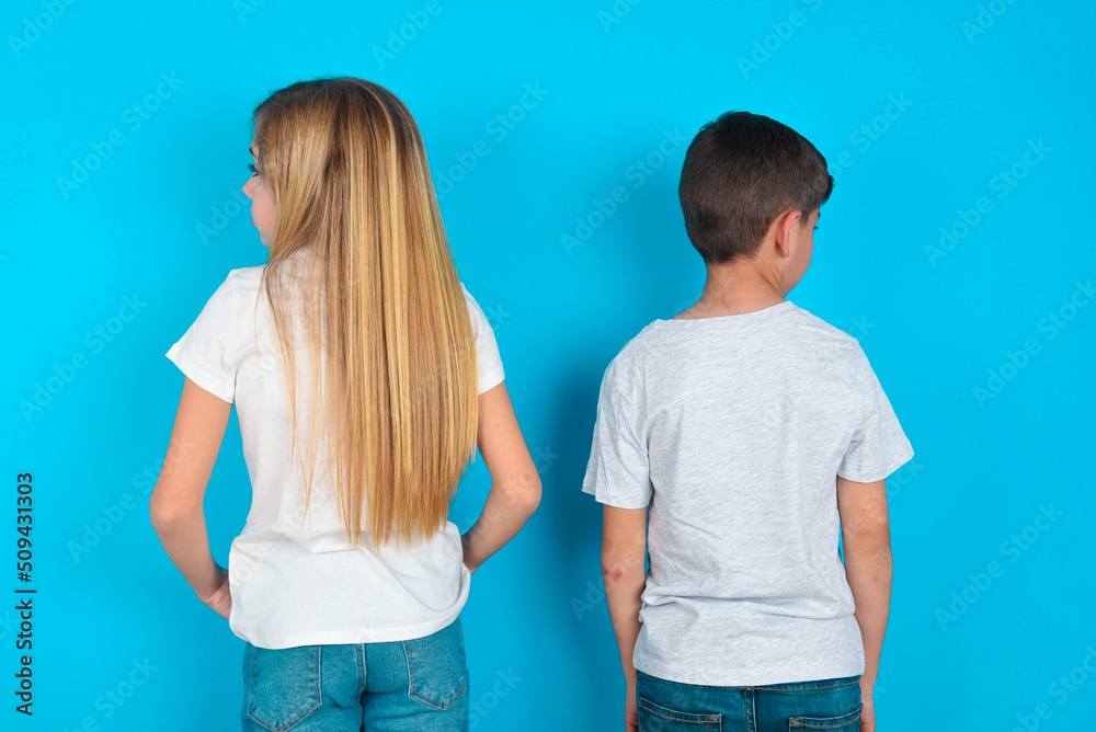 The back view of two kids boy and girl standing over blue studio ...