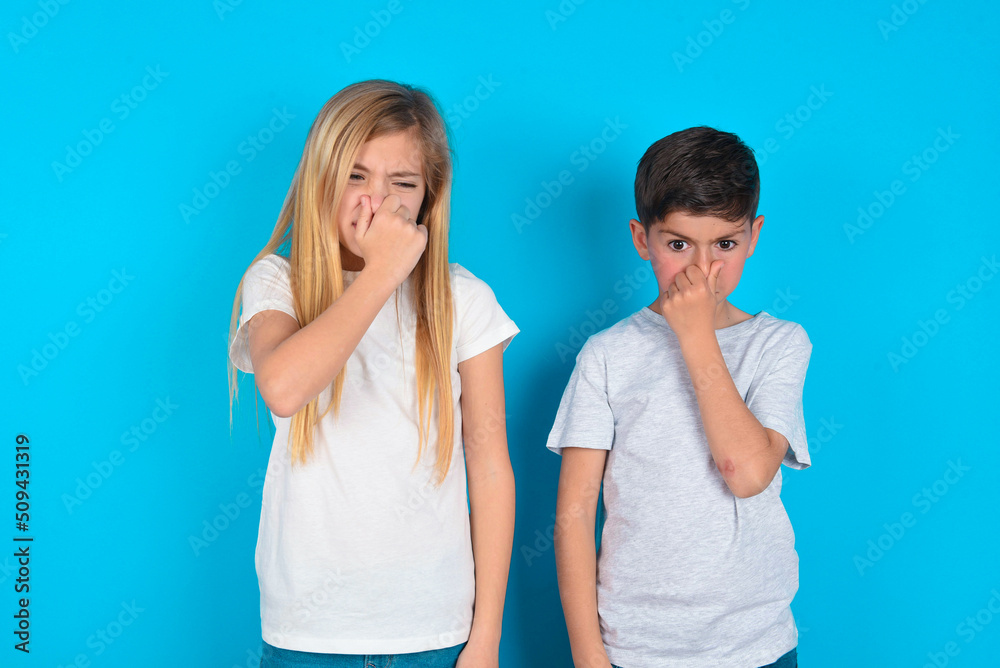 two kids boy and girl standing over blue studio background, holding his ...