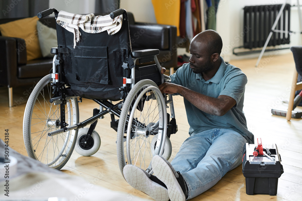 African man with disability sitting on floor and fixing his broken ...